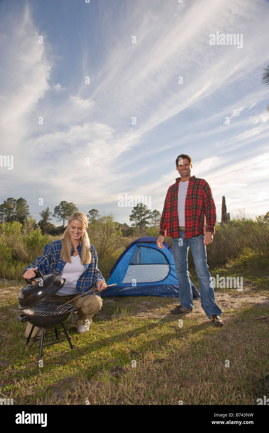 Couple by tent, woman preparing food on barbecue at campsite Stock ...