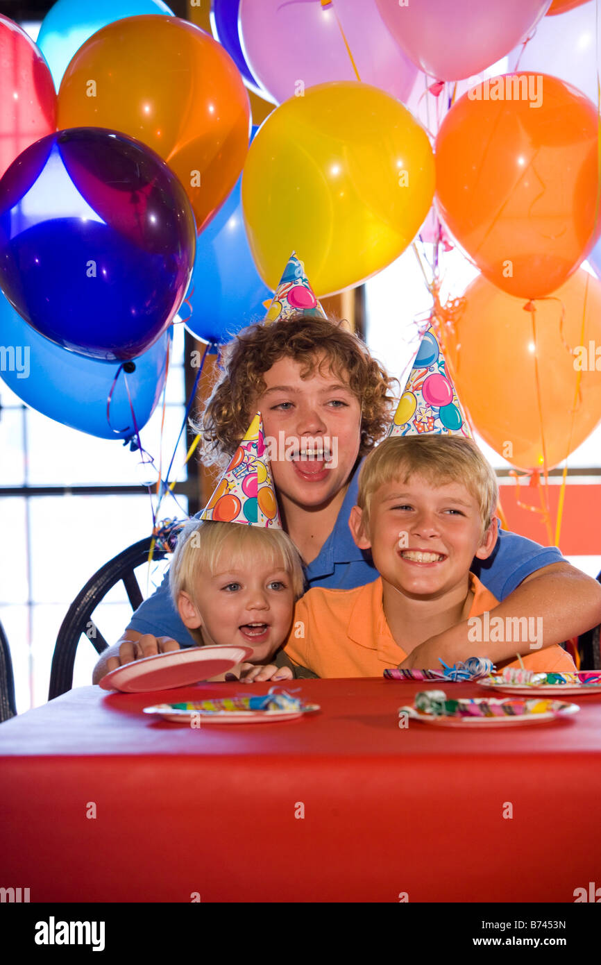 Three brothers posing at kids birthday party with lots of balloons ...