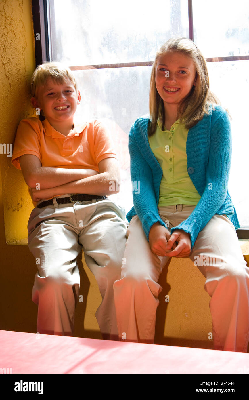 Portrait of two children sitting inside on window sill Stock Photo - Alamy