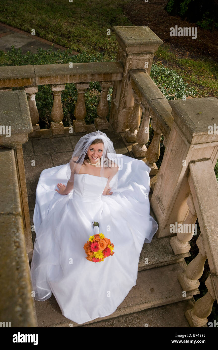Happy young bride in wedding dress sitting on stairs outside Stock ...