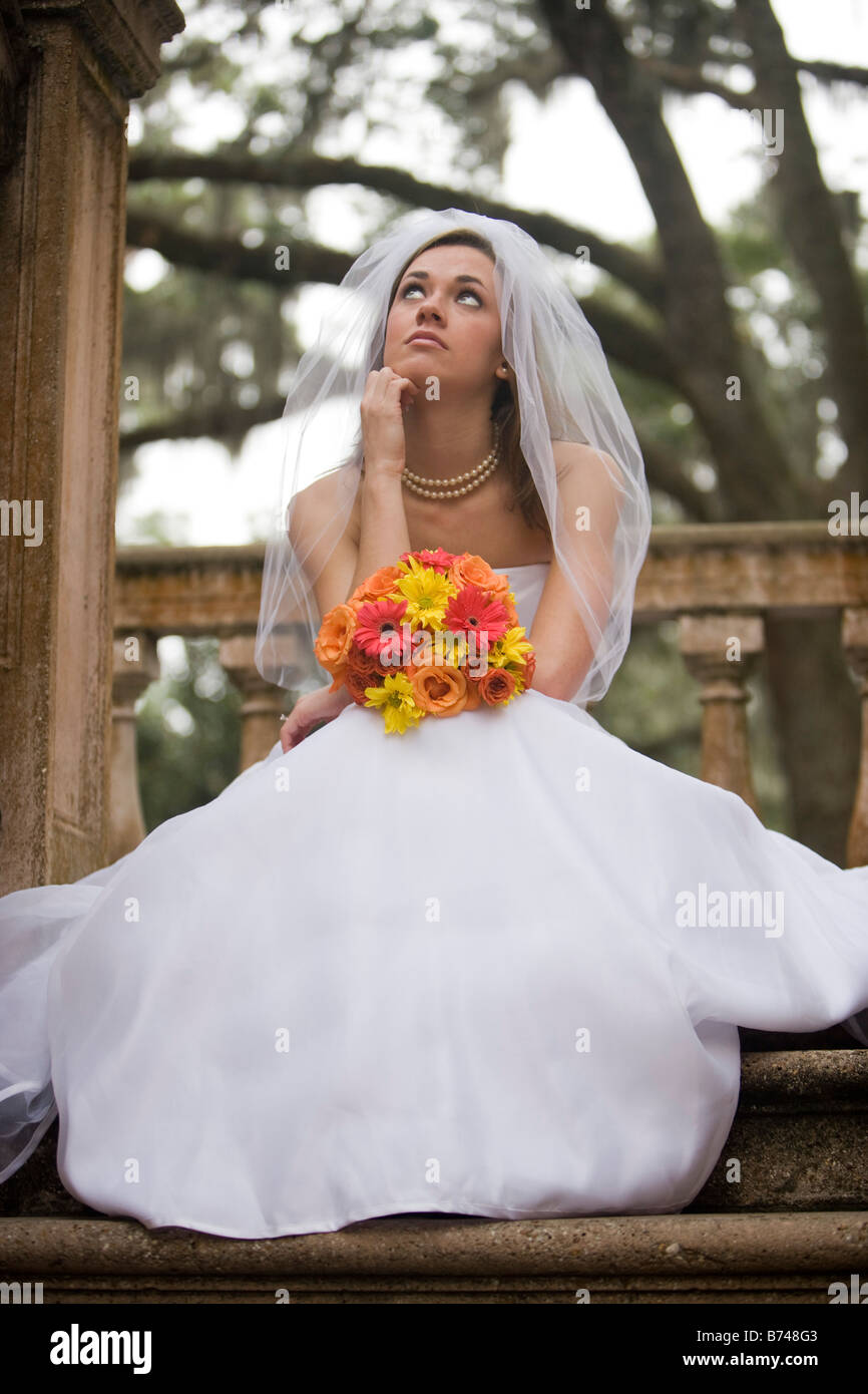 Young bride sitting outside at top of stairs on wedding day and ...