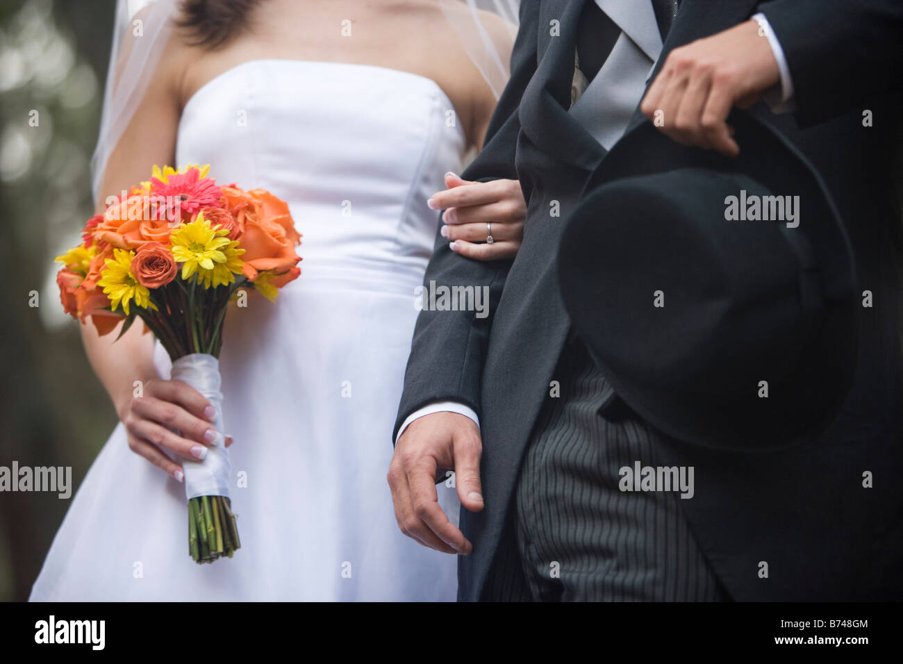 Midsection of bride and groom walking arm in arm holding bridal bouquet ...