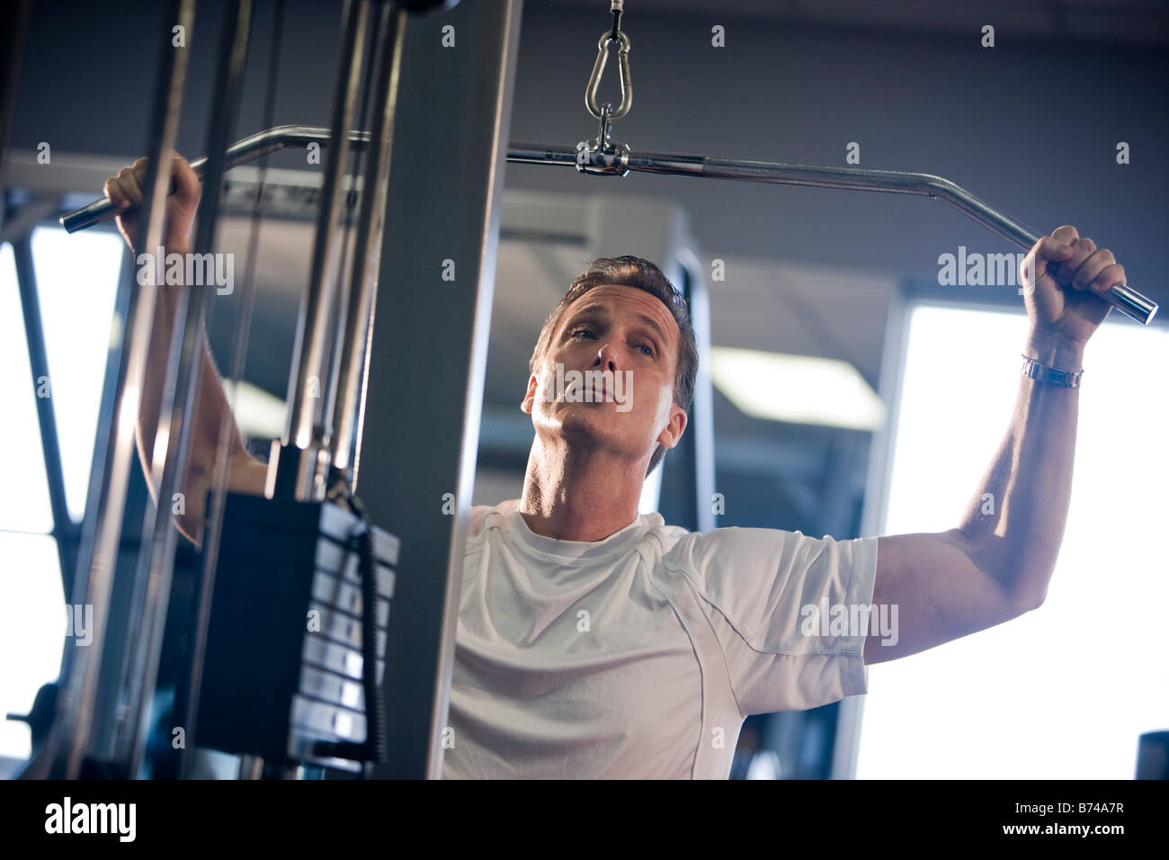 Middle-aged man pulling weight machine at gym Stock Photo - Alamy