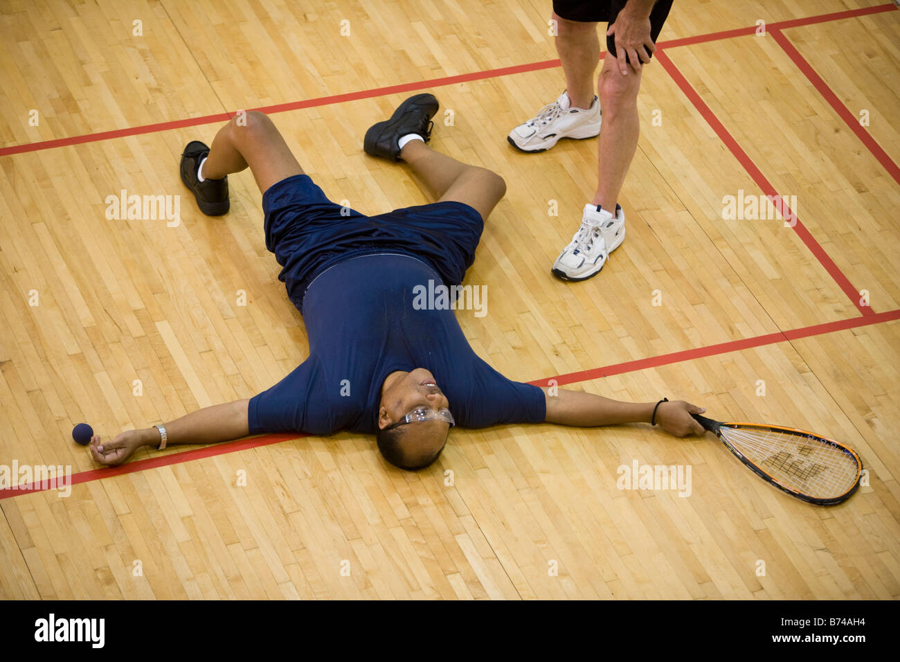 Senior man playing dead on racketball court at feet of opponent Stock ...