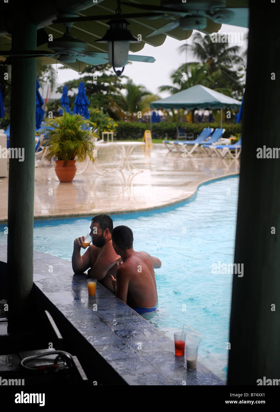 TWO TOURISTS SIT AT THE POOL BAR DURING A RAIN STORM AT A CARIBBEAN ...