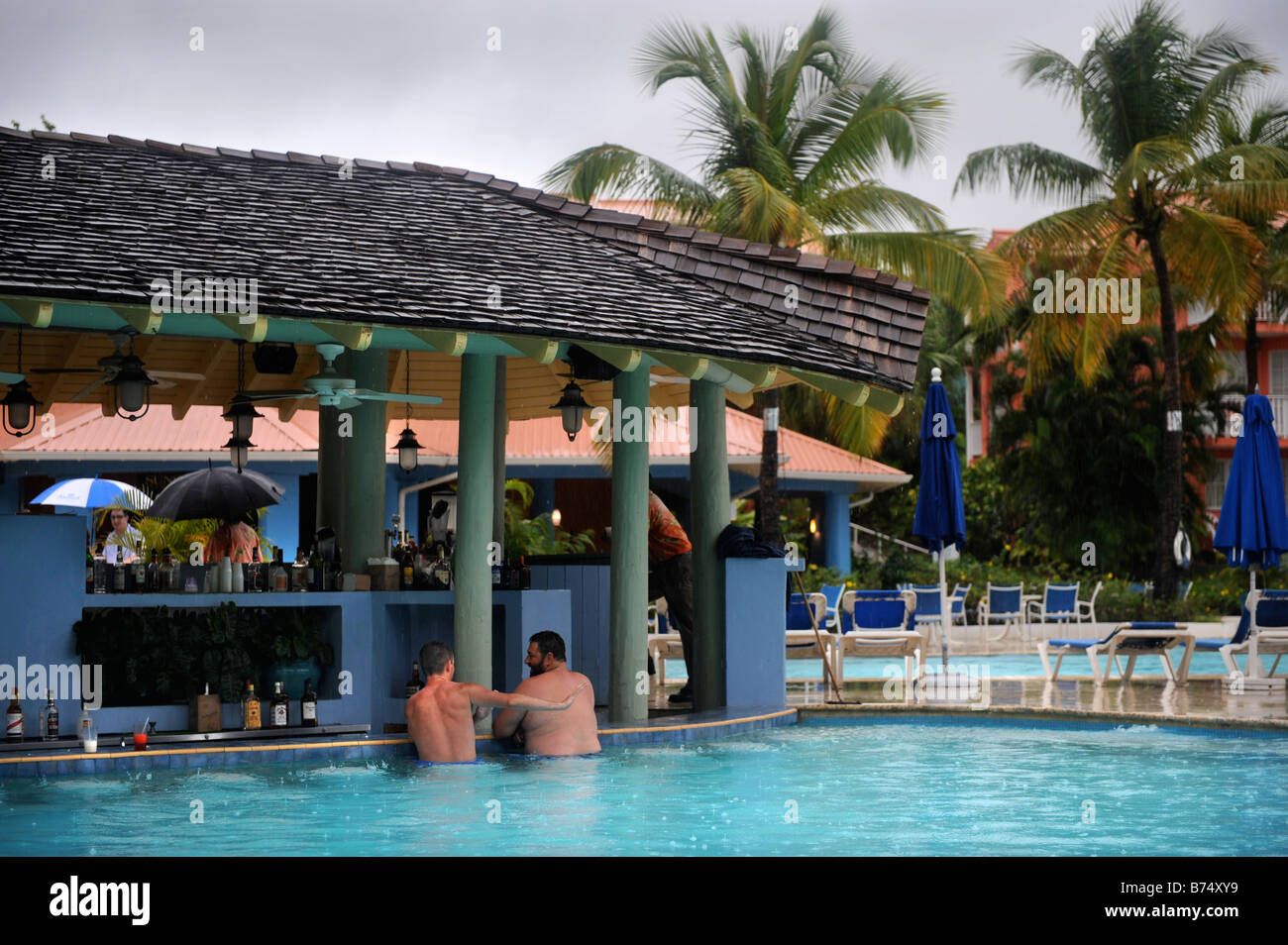 TWO TOURISTS SIT AT THE POOL BAR DURING A RAIN STORM AT A CARIBBEAN ...