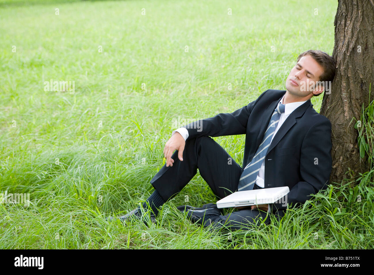One mid adult man leaning against tree sleeping Stock Photo - Alamy
