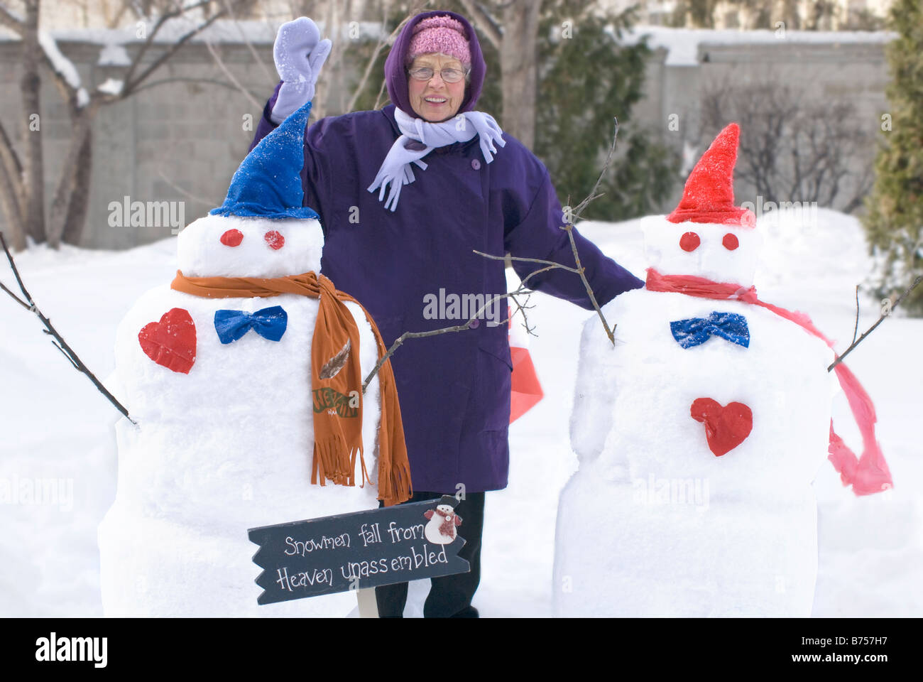 Senior woman waving beside snowman that she made, Winnipeg, Canada ...