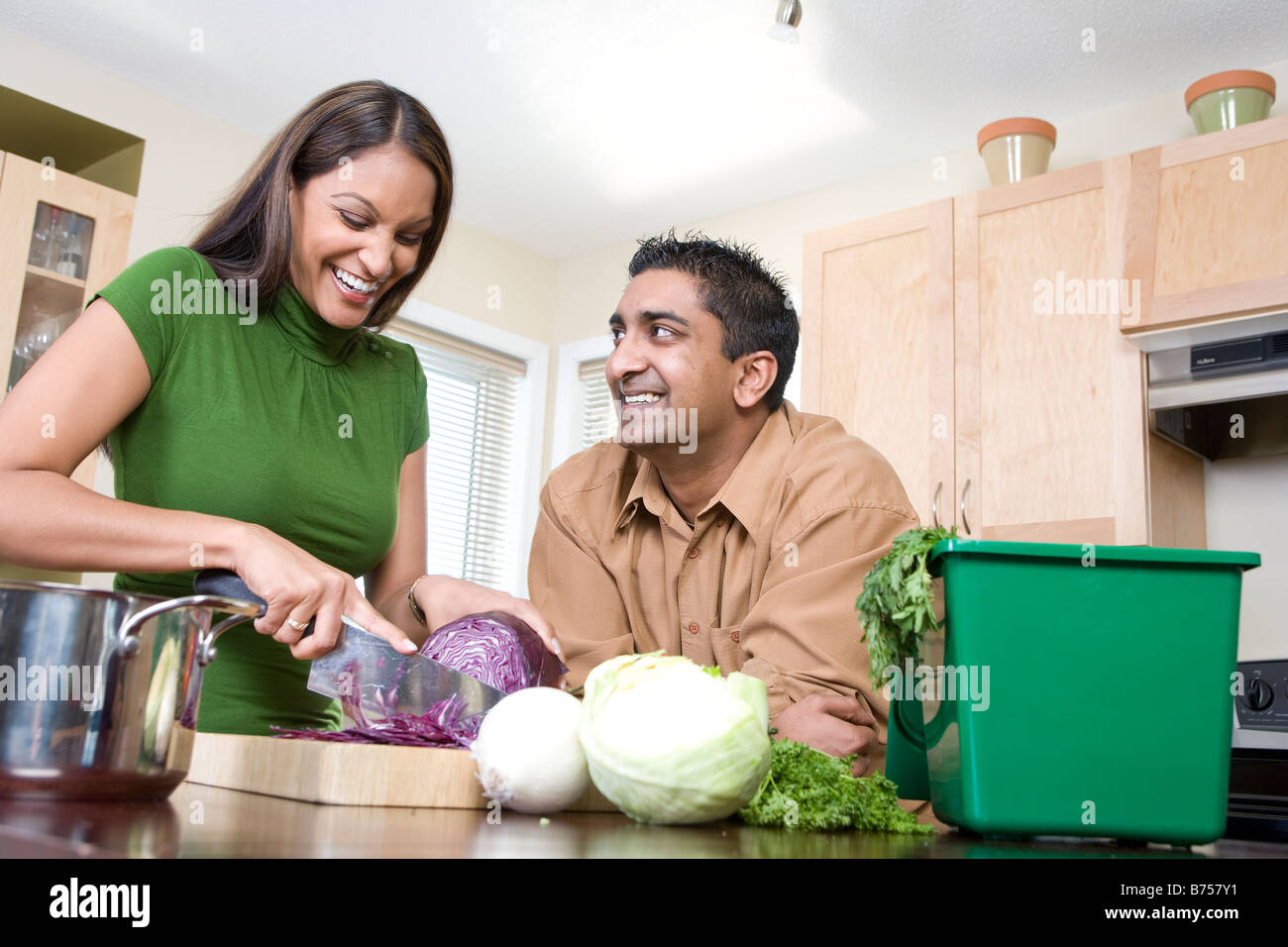 Couple in kitchen cutting vegetables beside kitchen compost bin ...