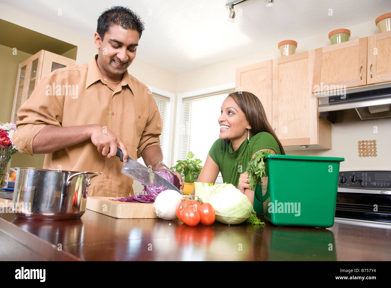 Couple in kitchen cutting vegetables beside kitchen compost bin ...