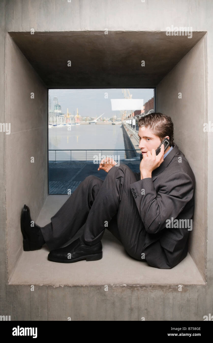Side profile of a businessman sitting on a window sill and talking on a ...