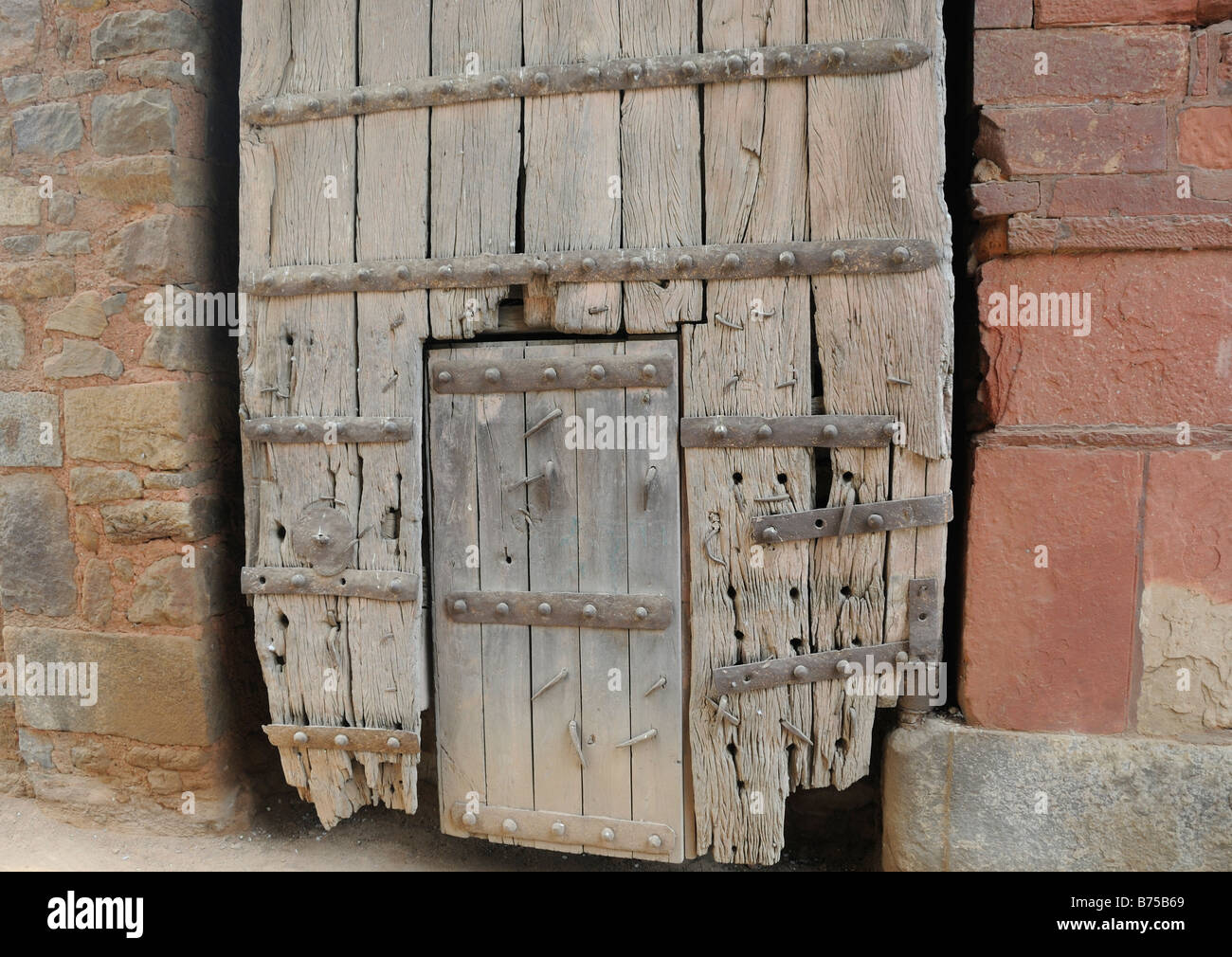 An ancient wooden door with iron studs and bands and a small posten ...