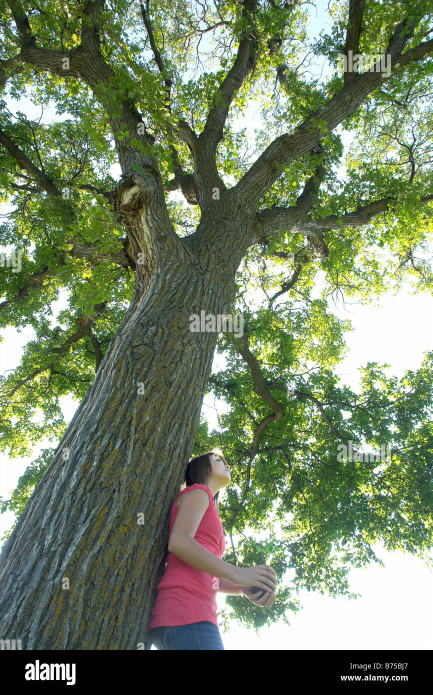 Thirteen year old girl holding small tree stands beside larger tree ...