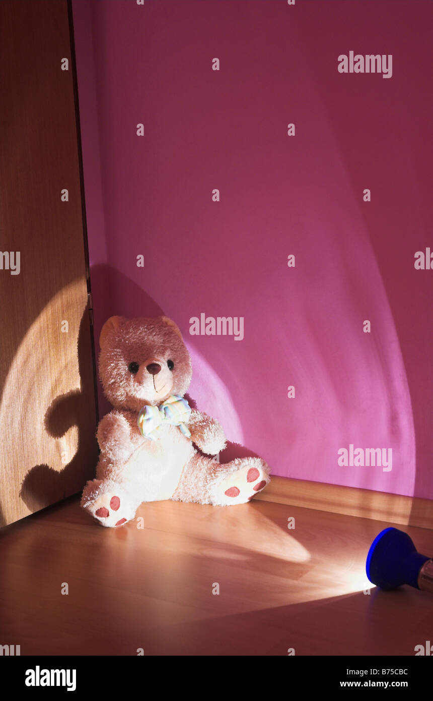 Teddy bear sitting on floor in corner of a room with flashlight shining ...