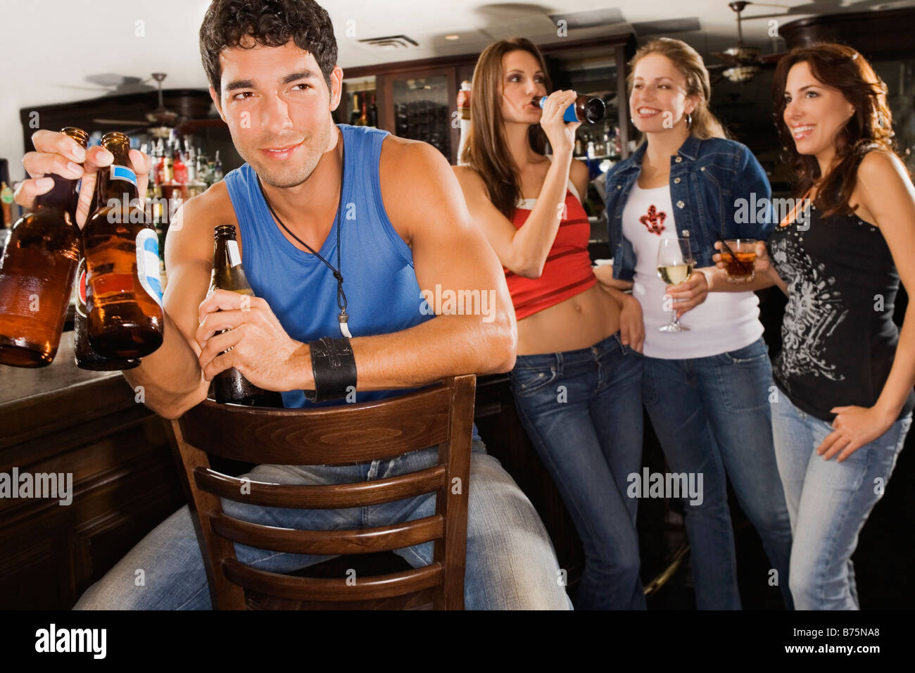 Young man sitting at a bar counter with his three friends standing ...