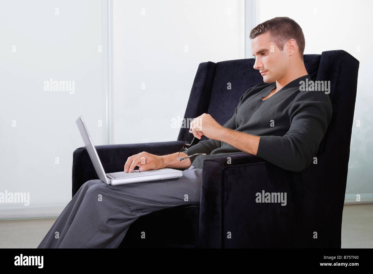 Side profile of a young man sitting in an armchair and working on a ...