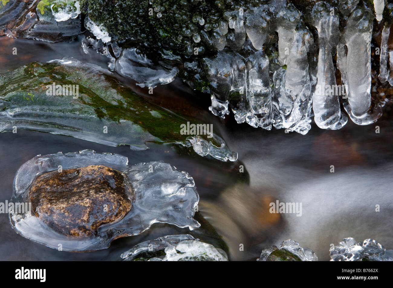Ice formed on rocks in a mountain stream with water rushing past Stock ...