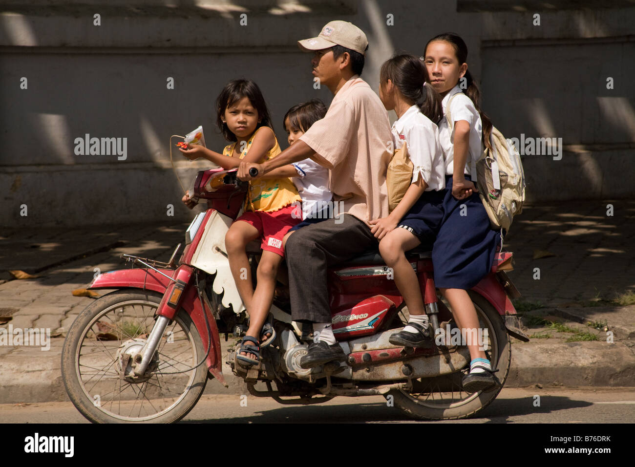 A moped with five people on it in Phnom Penh, four kids, one in school ...