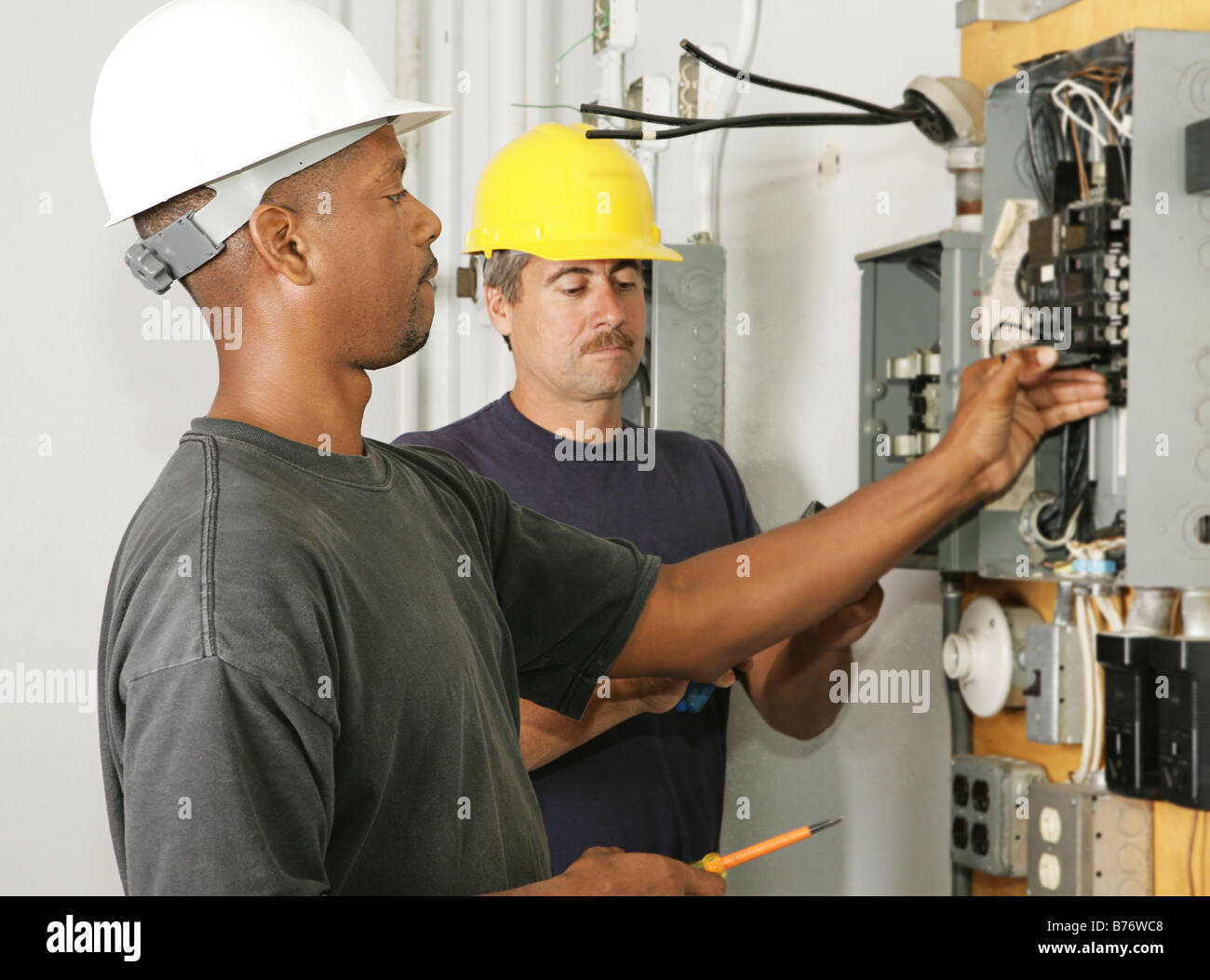 An african american and a caucasian electrician working on a panel ...