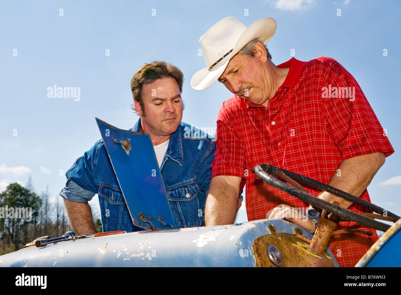Rancher and ranch hand working together to repair the tractor Stock ...