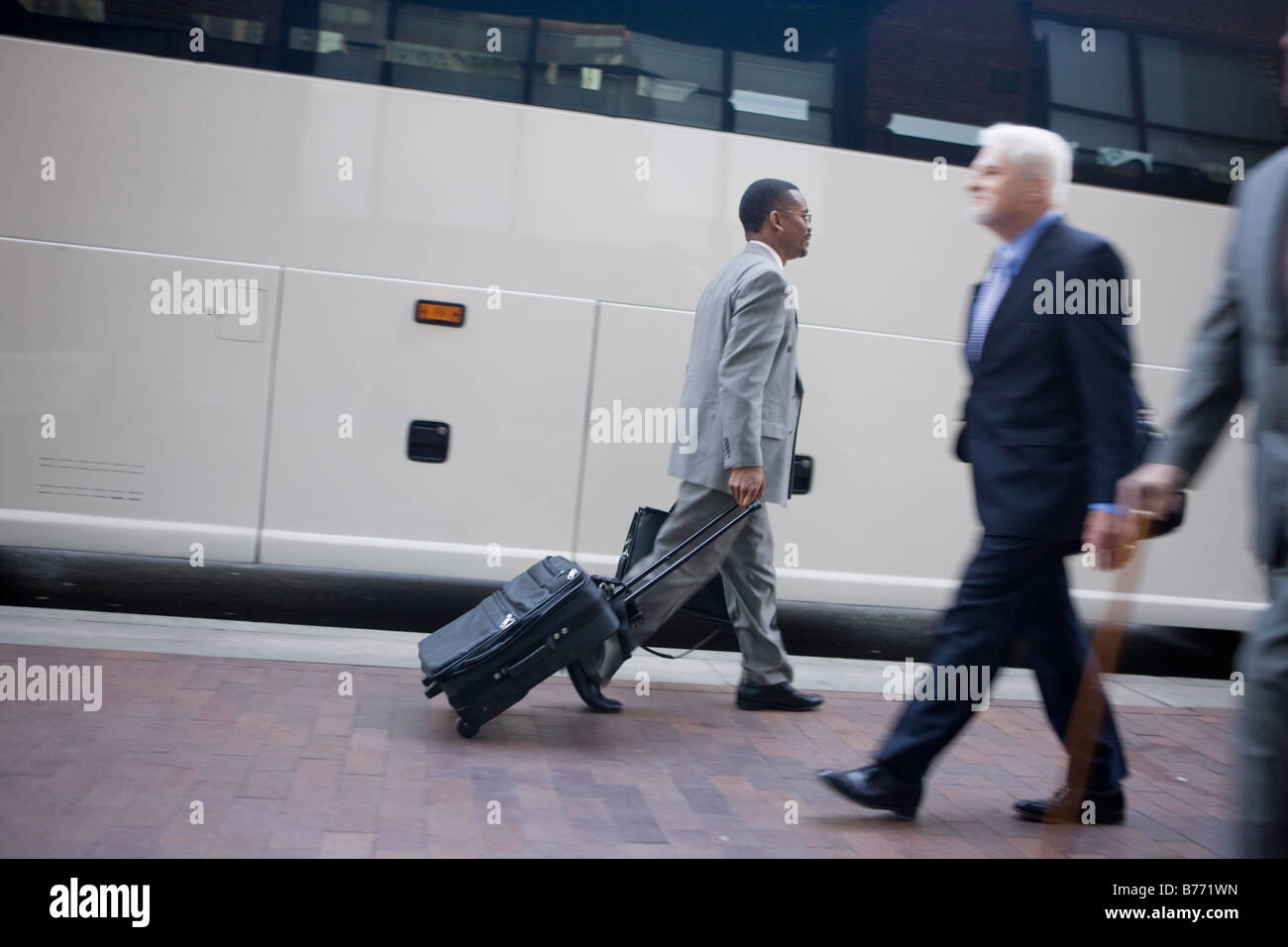 Businessman pulling luggage along bus Stock Photo - Alamy