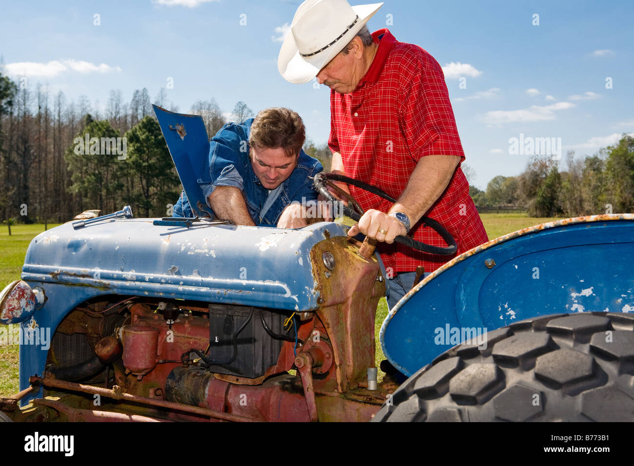 Farmer and ranch hand work on repairing the old tractor together Stock ...