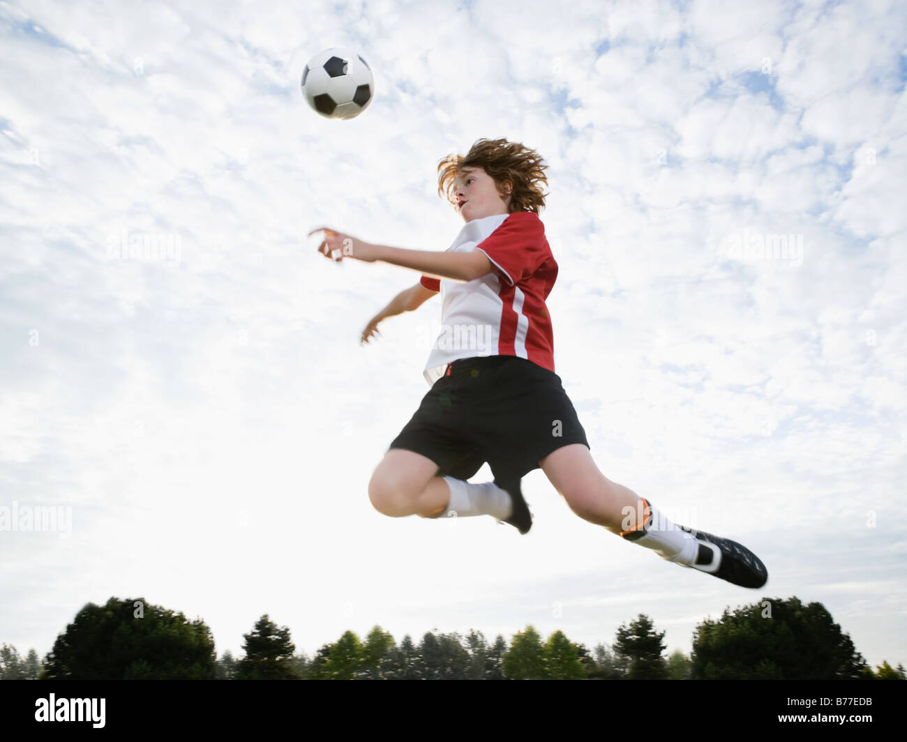 Boy jumping toward soccer ball mid-air Stock Photo - Alamy