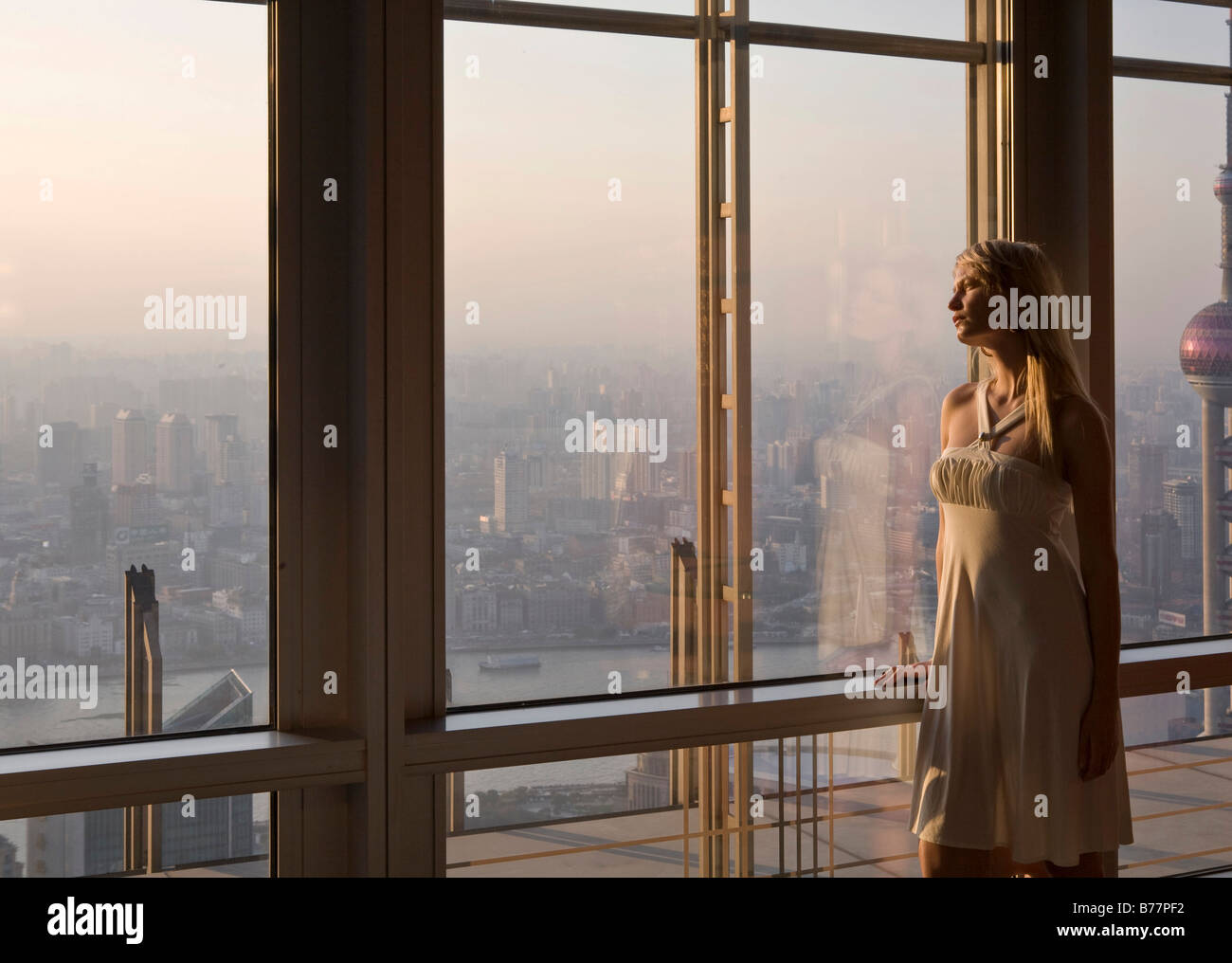 Young woman looking at the skyline through her window, Shanghai, China ...