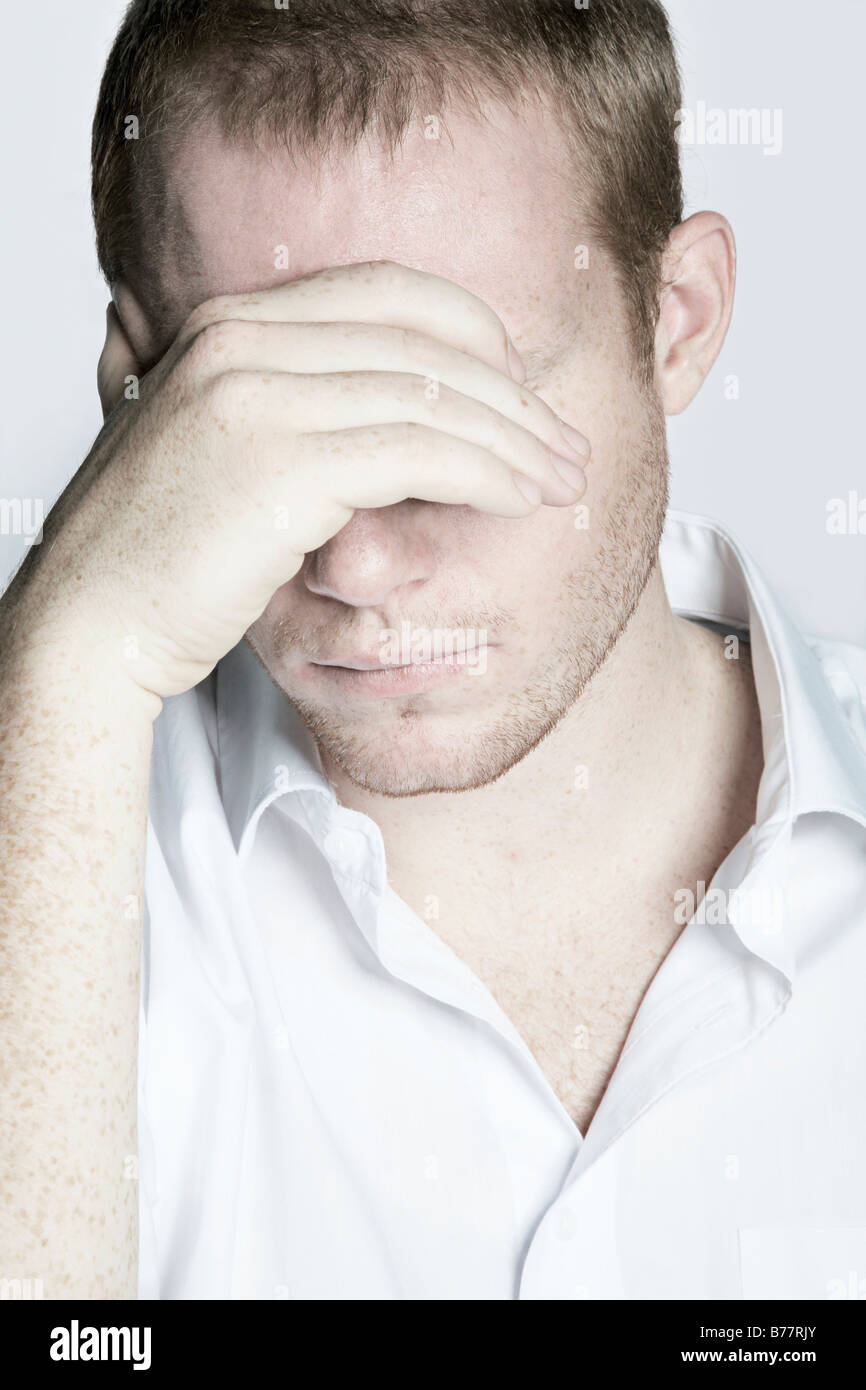 Pensive young man holding his hand to his forehead Stock Photo - Alamy