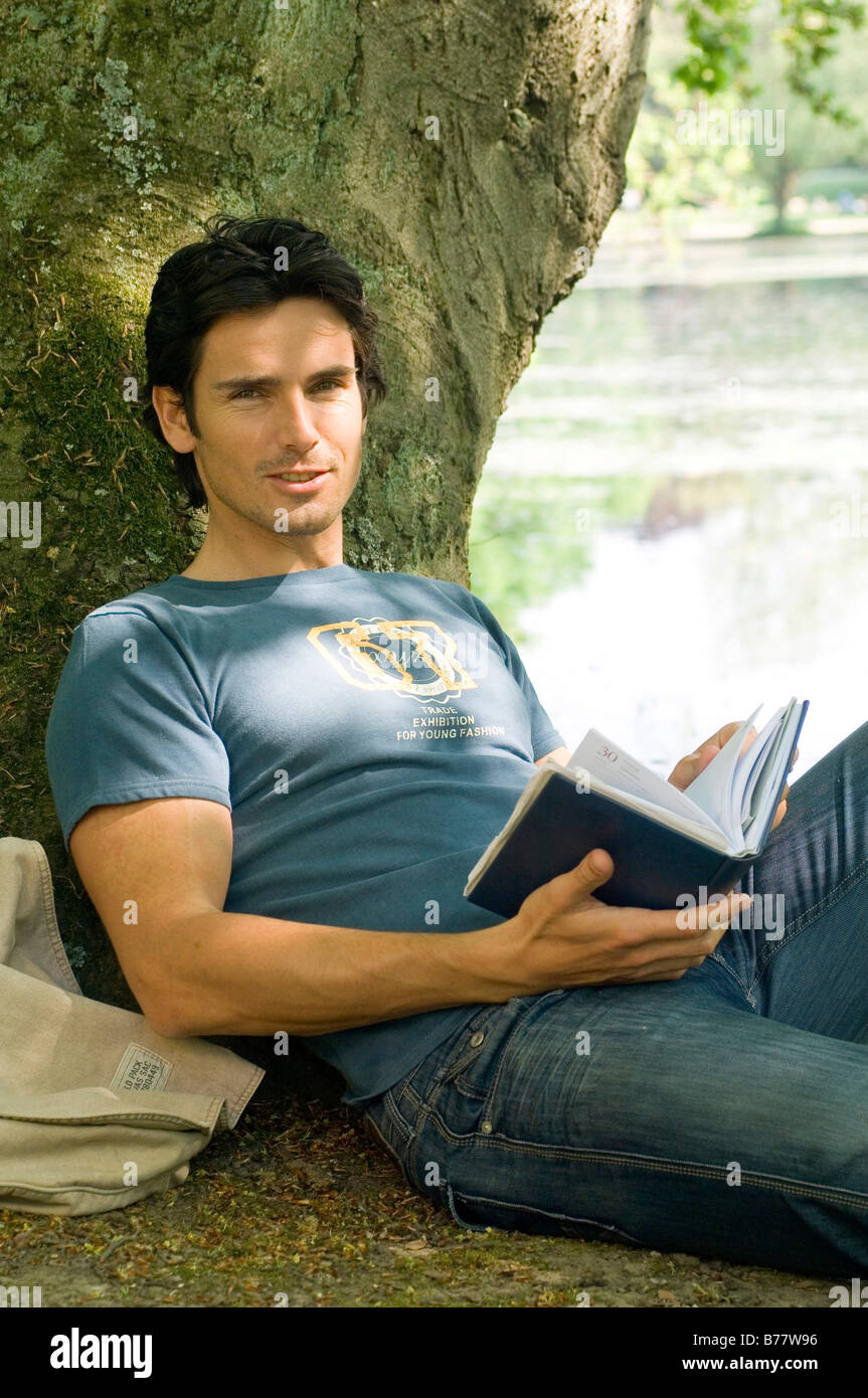 Man sat down leaning against a tree reading a book Stock Photo - Alamy