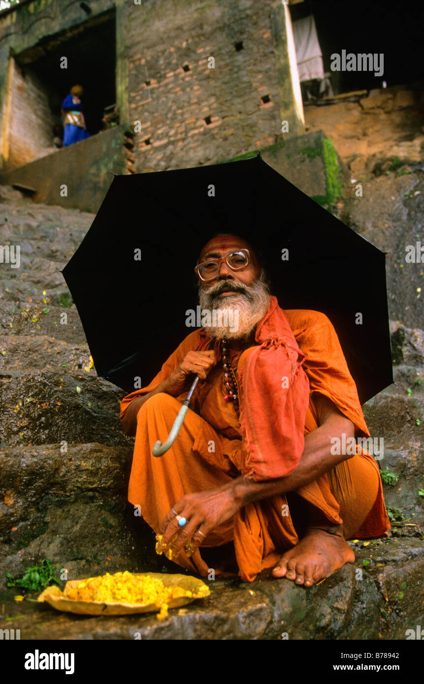 A priest clad in red and saffron, eats a meal on the steps while ...