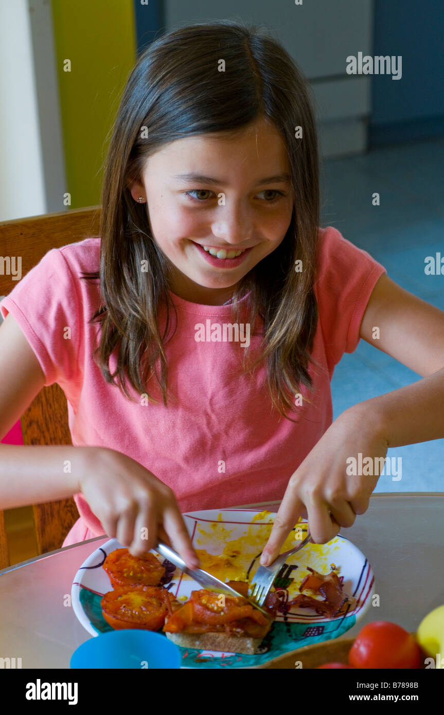 Young girl eating a breakfast of bacon eggs and fried tomatoes on toast ...