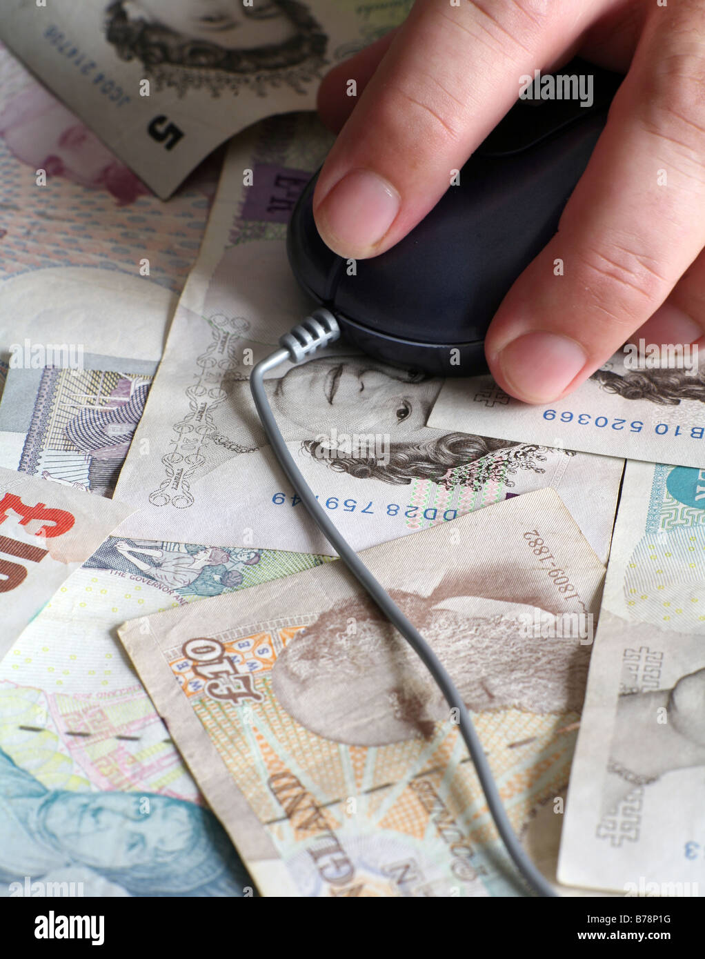 Fingers on a computer mouse over an array of banknotes,symbolic of ...