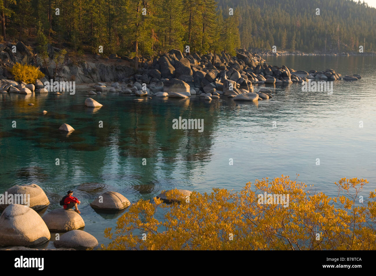 A man sitting on a rock on the shore of Lake Tahoe in California at ...