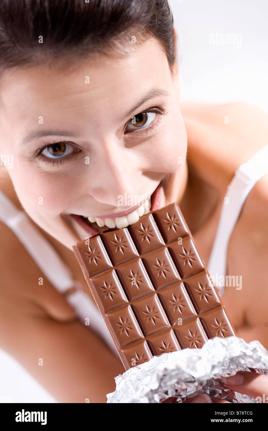 Young woman biting into chocolate bar, smiling Stock Photo - Alamy