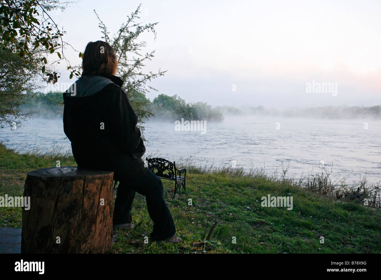 A guest looking out over the Zambezi river with rising mist at dawn at ...