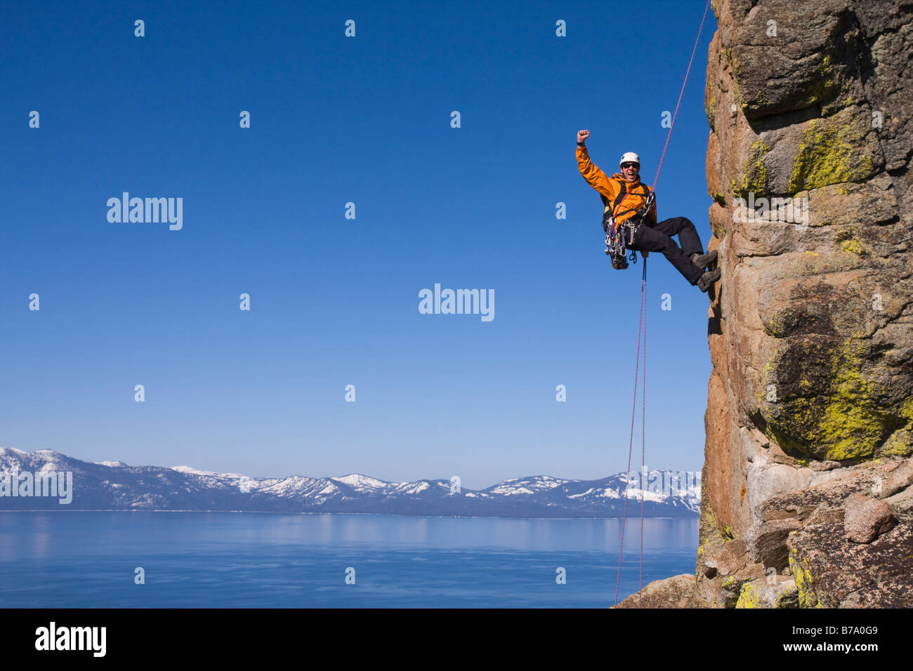 A man rappelling off a cliff and making the victory sign above Lake ...