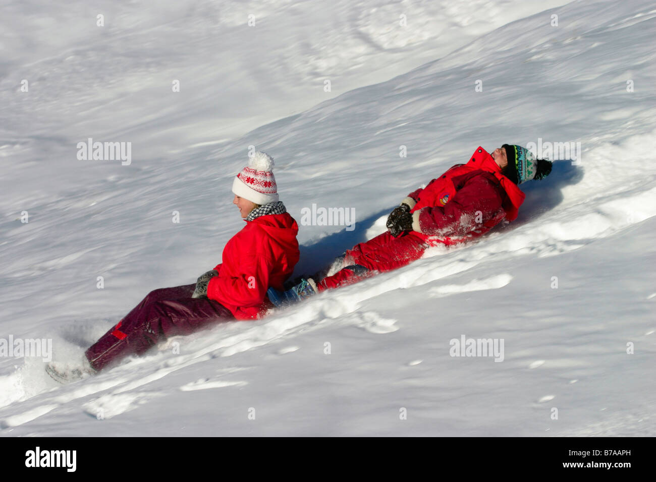 Two girls, 9 and 12 years old, riding on snow-sliders, Dolomites, Italy ...