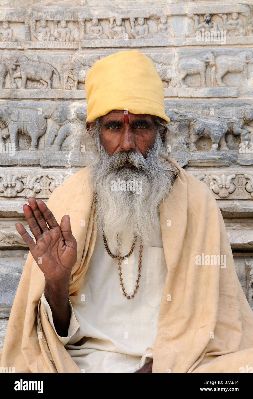 A bearded holy man poses in front of an intricately carved temple wall ...