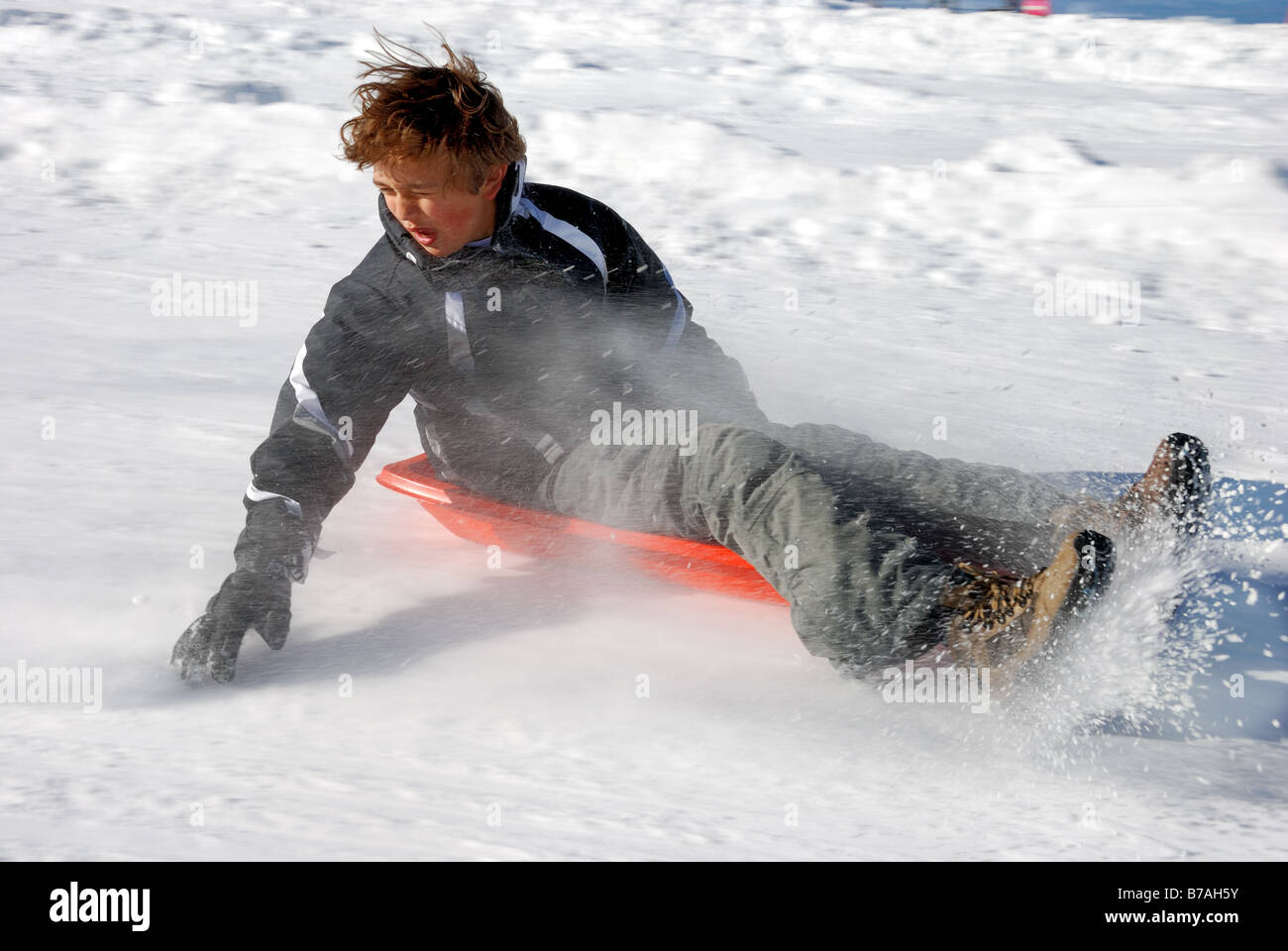 Boy braking with the sled while sledding down the hill with snow ...