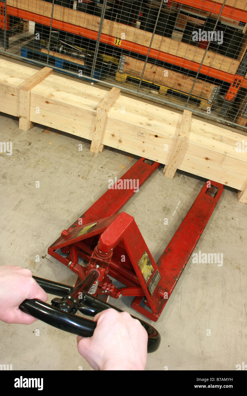 Man moving a wooden crate with a pallet truck in a UK warehouse Stock ...