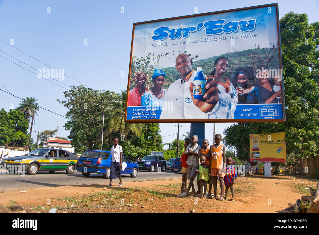 Children stand under a billboard advertising Sur'Eau on a busy street ...