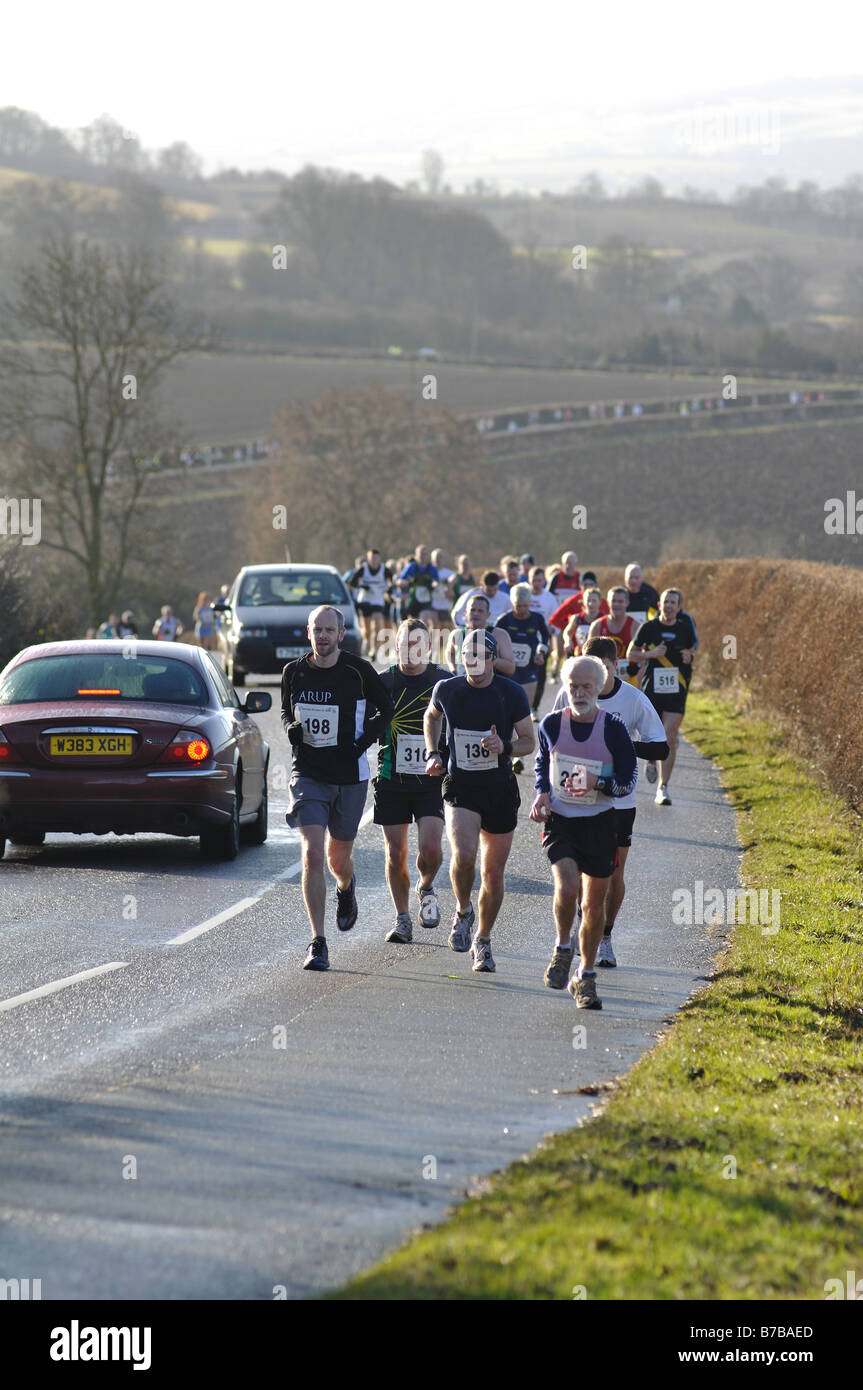 Runners in a road race with cars passing, Loxley, Warwickshire, UK ...