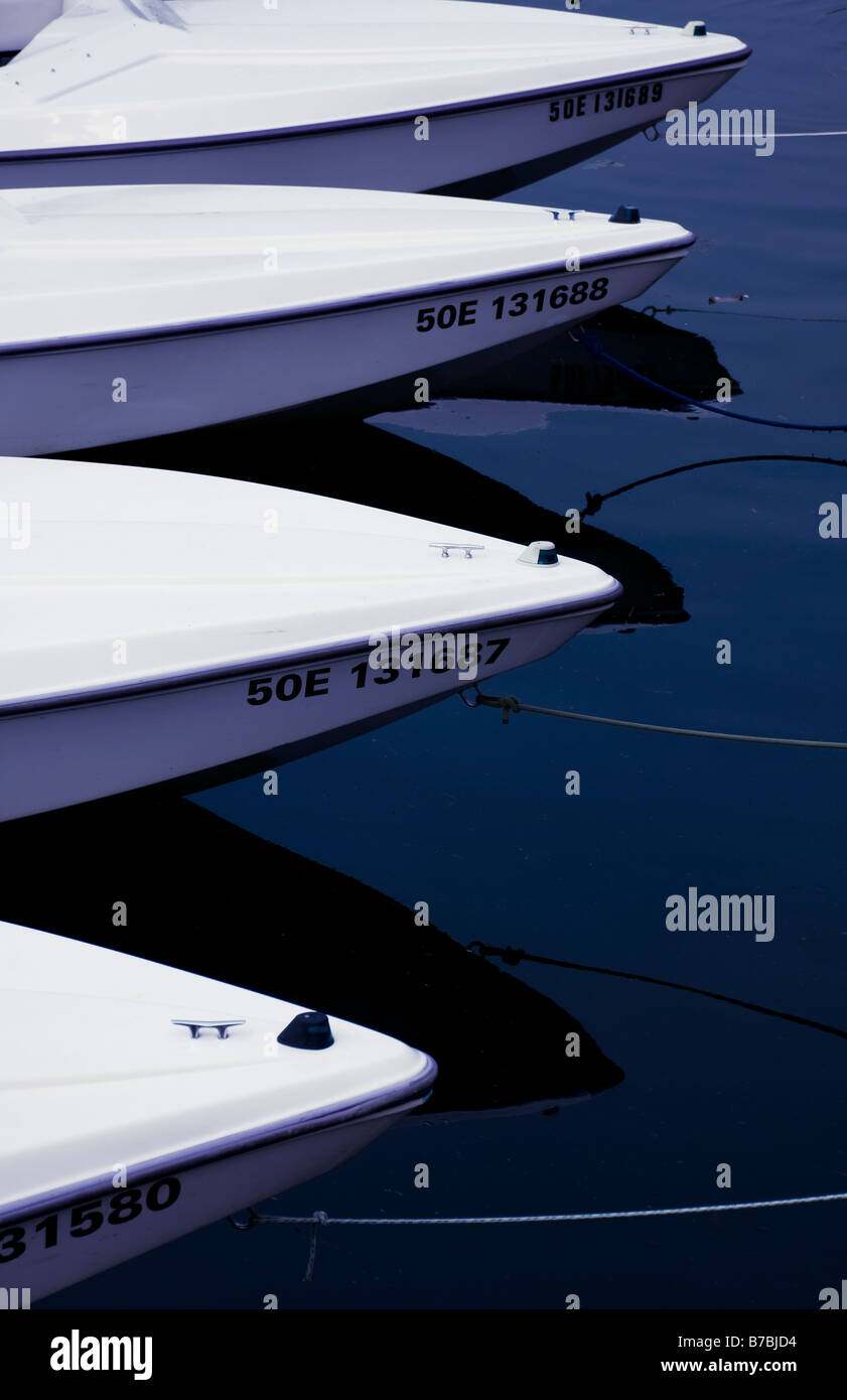 The bows of four white boats lined up floating on dark blue water. Rope ...