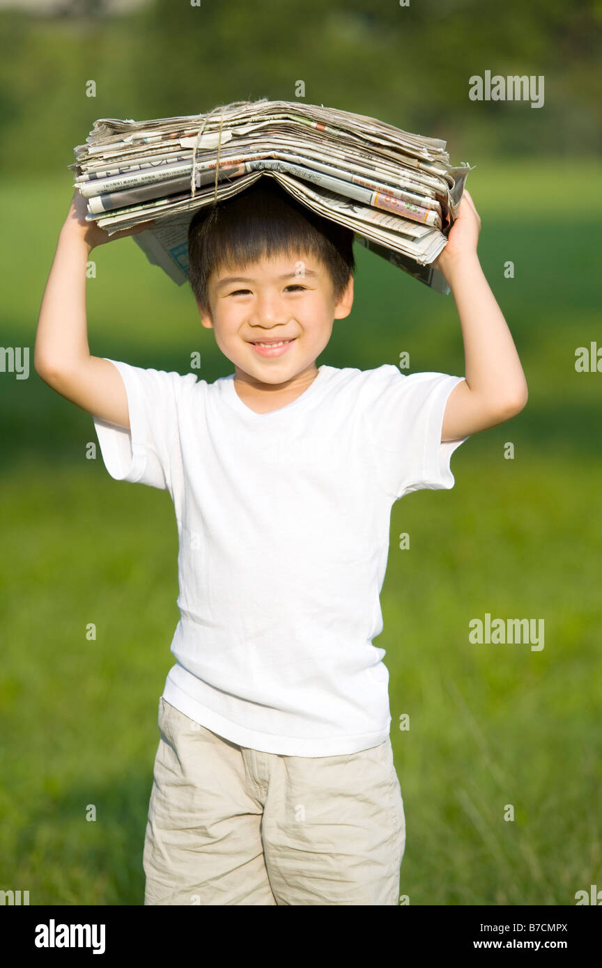 Little boy holding stack of newspaper on the head and looking at the ...