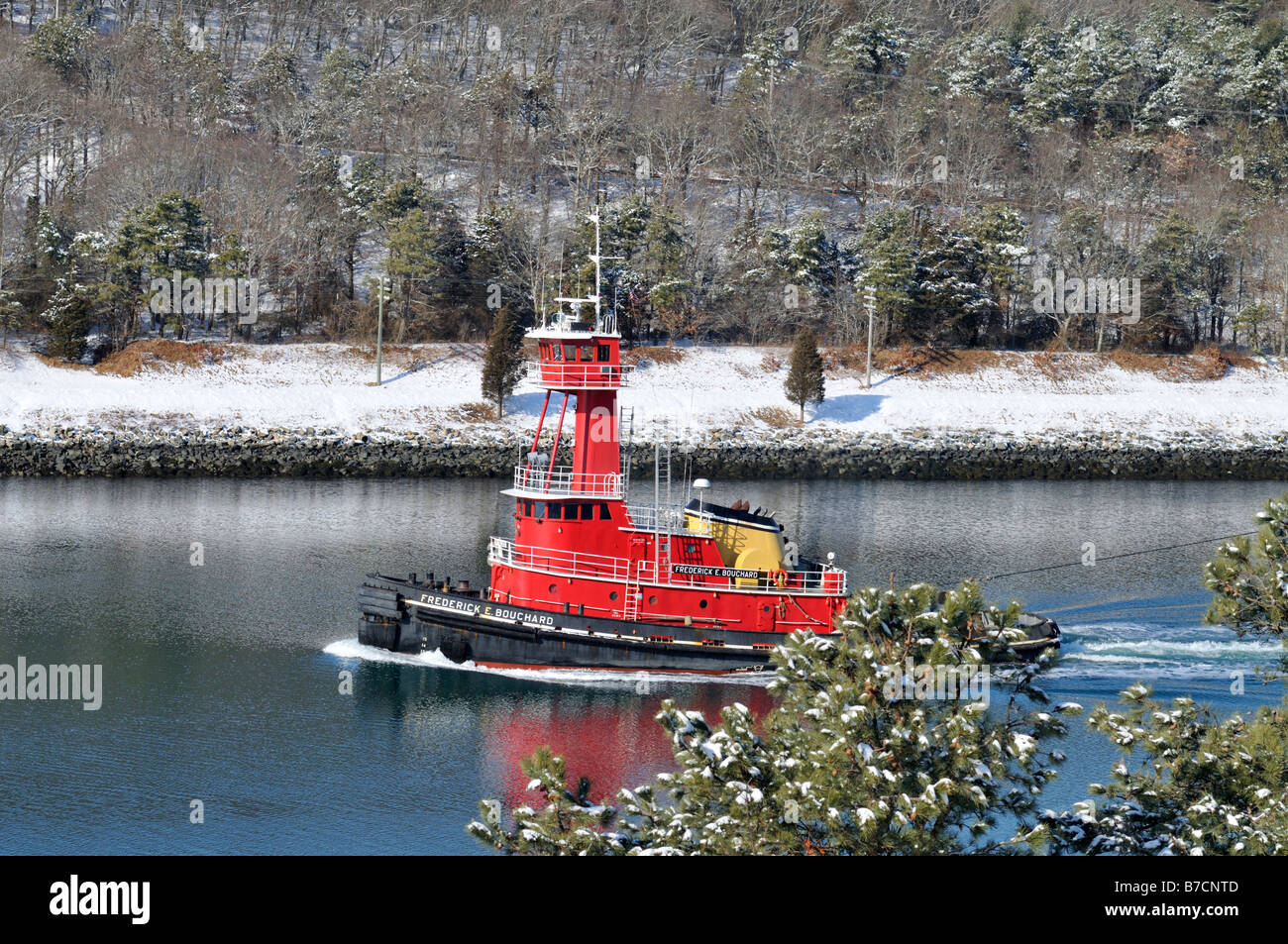 Winter scenic with cruising red tugboat water snow and evergreen trees ...