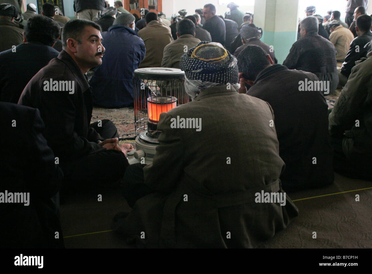 Kurdish Muslims praying in mosque , warming up hands with gas heaters ...