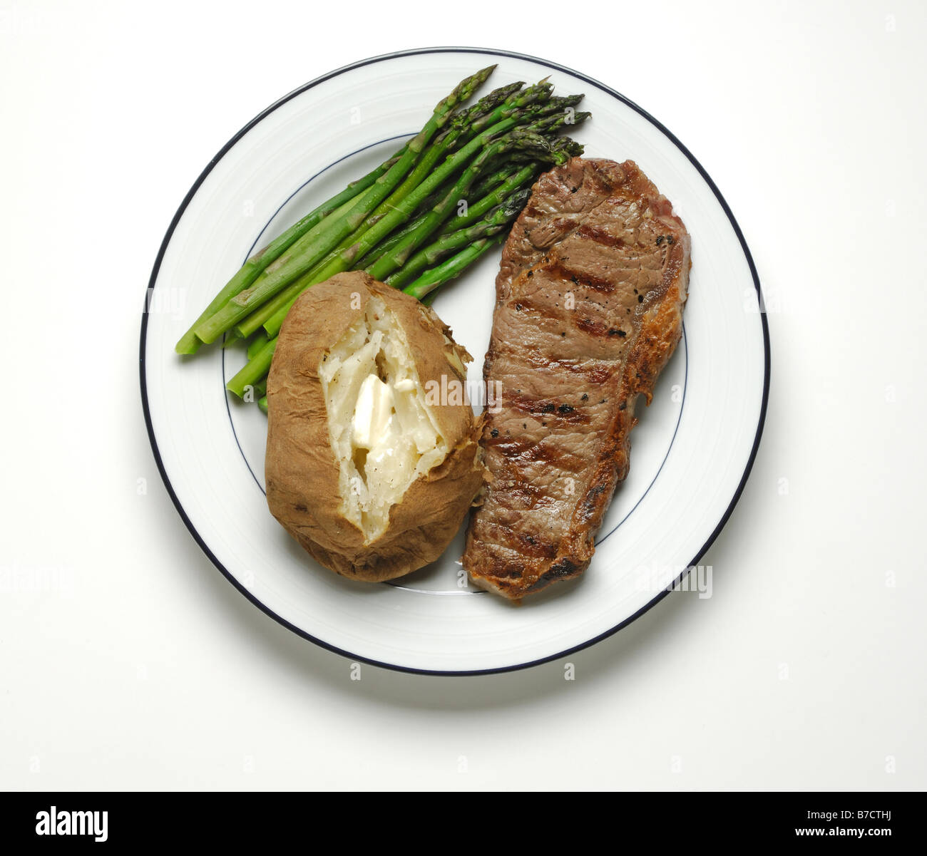 A cooked strip beef steak with asparagus stalks and a baked potato with ...