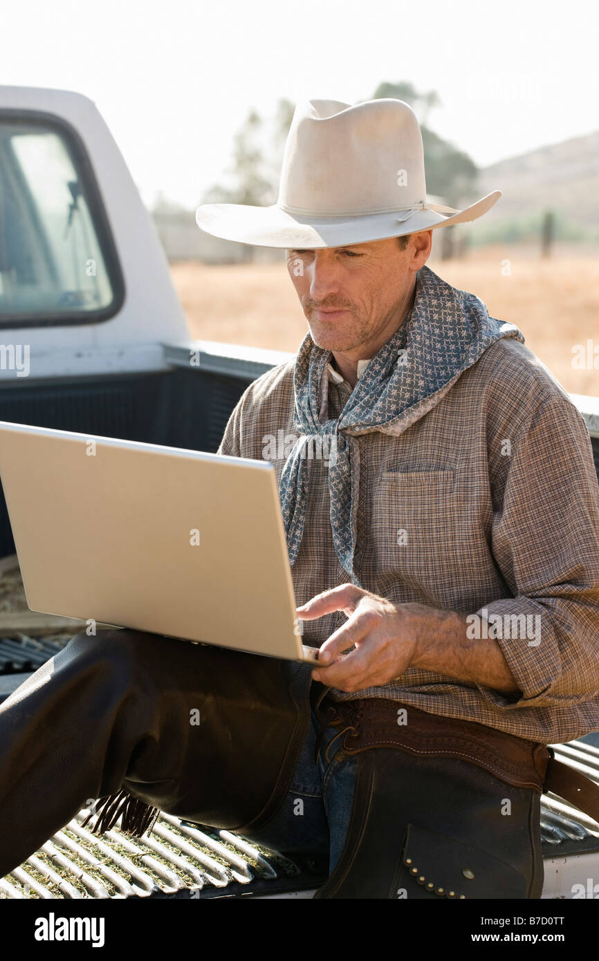 A cowboy sitting on the back on a truck and using his laptop Stock ...