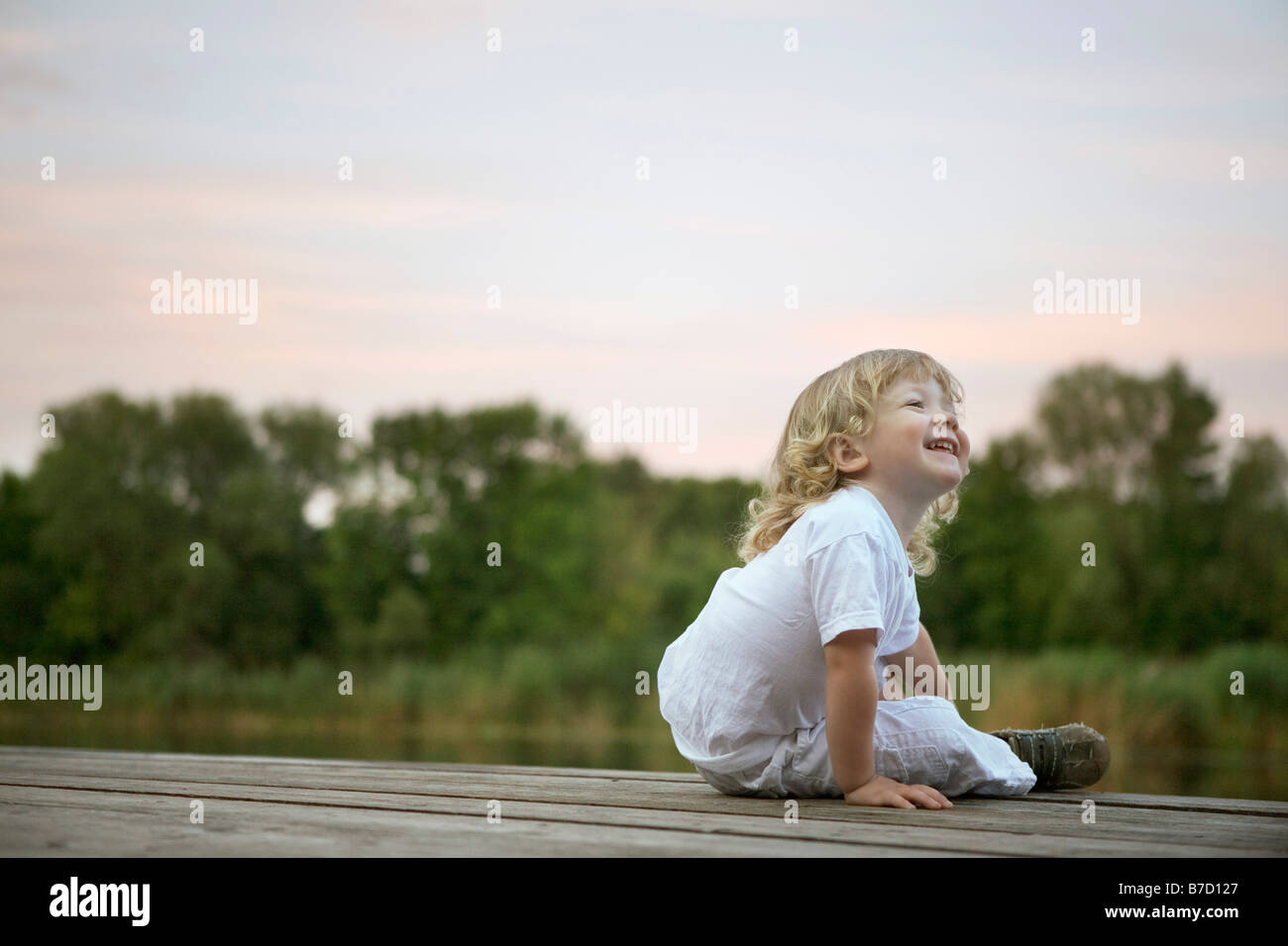 A laughing boy sitting on a jetty Stock Photo - Alamy